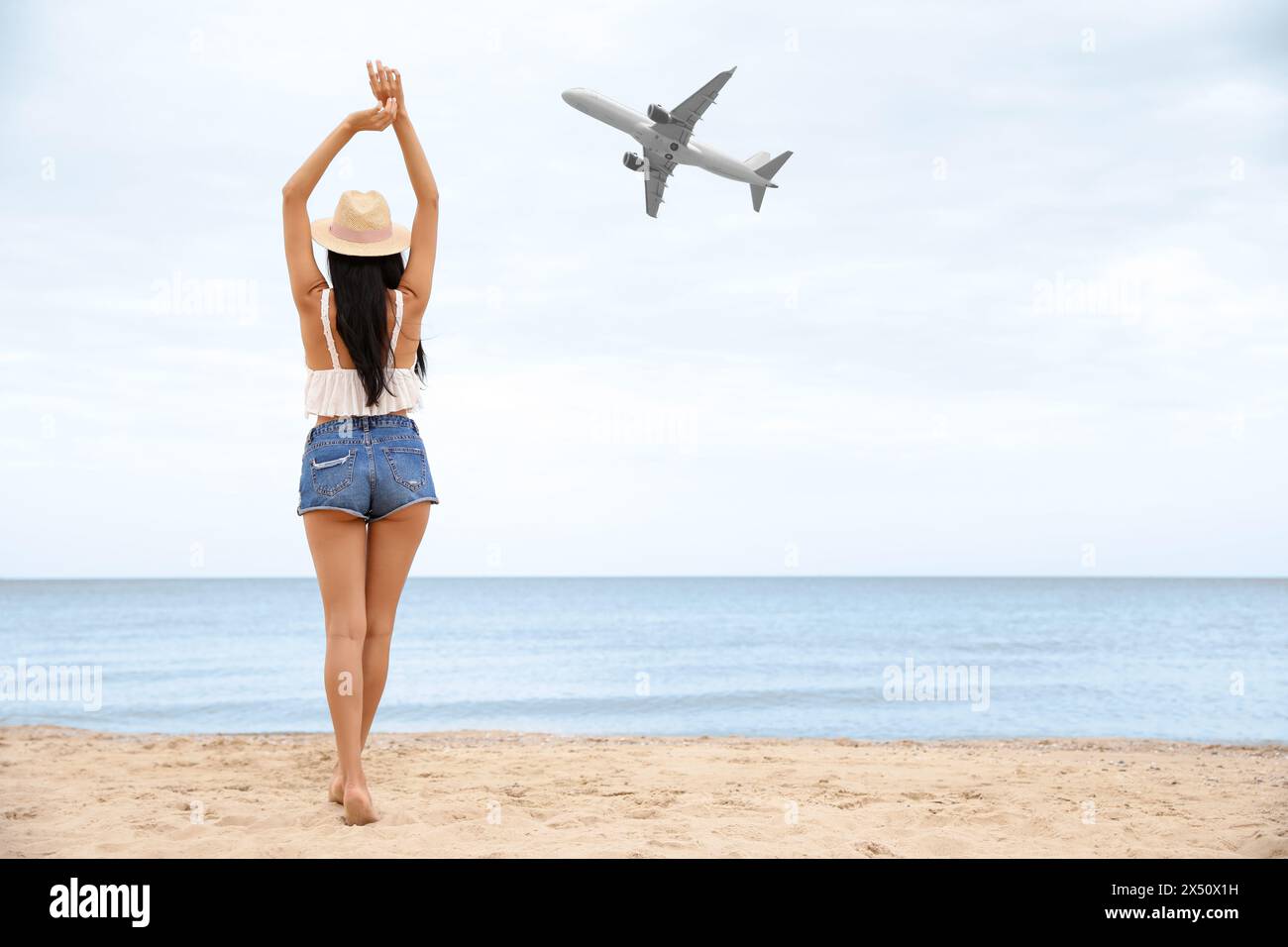 Woman on beach looking at airplane flying in sky, back view Stock Photo ...