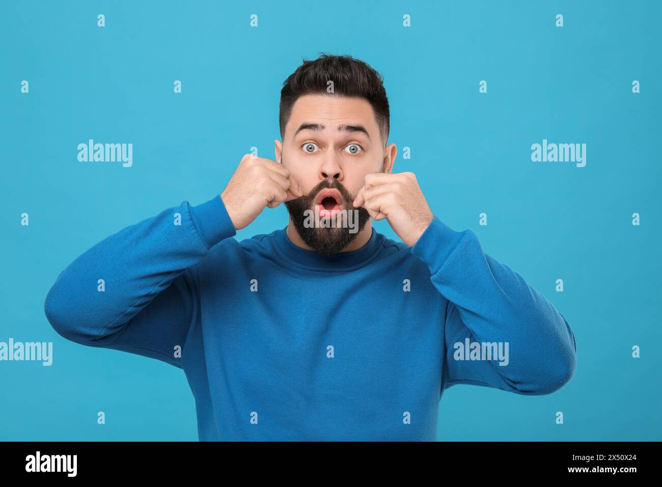 Surprised young man touching mustache on light blue background Stock ...