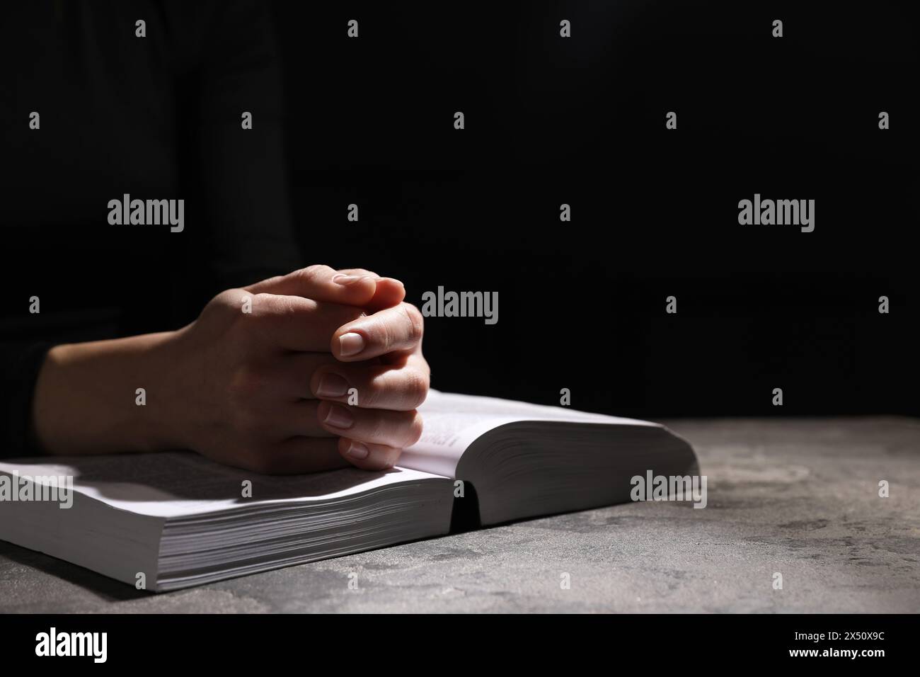 Religion. Christian woman praying over Bible at table against black ...