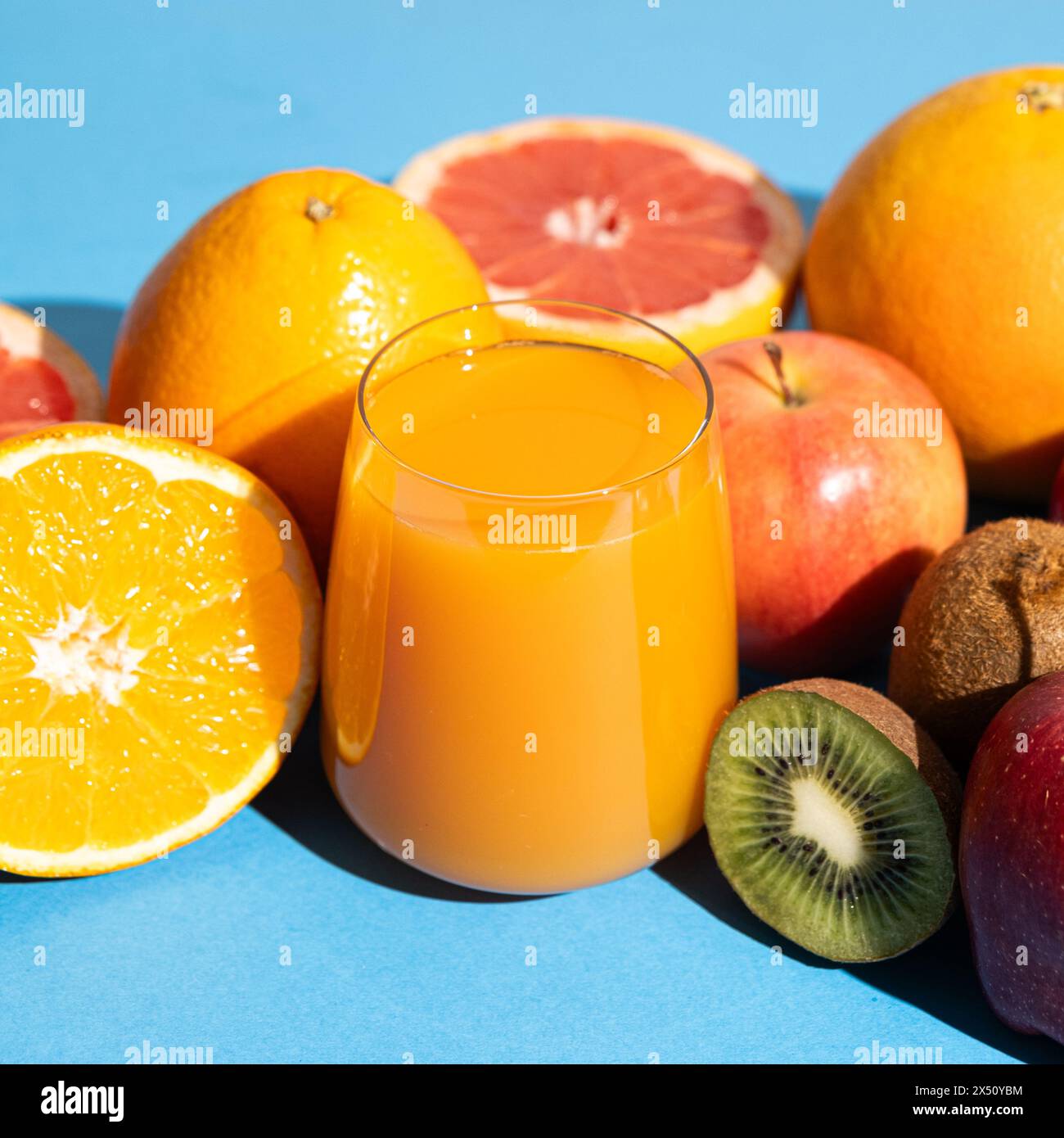 Multifruit juice in a glass among fresh fruits on blue background Stock ...
