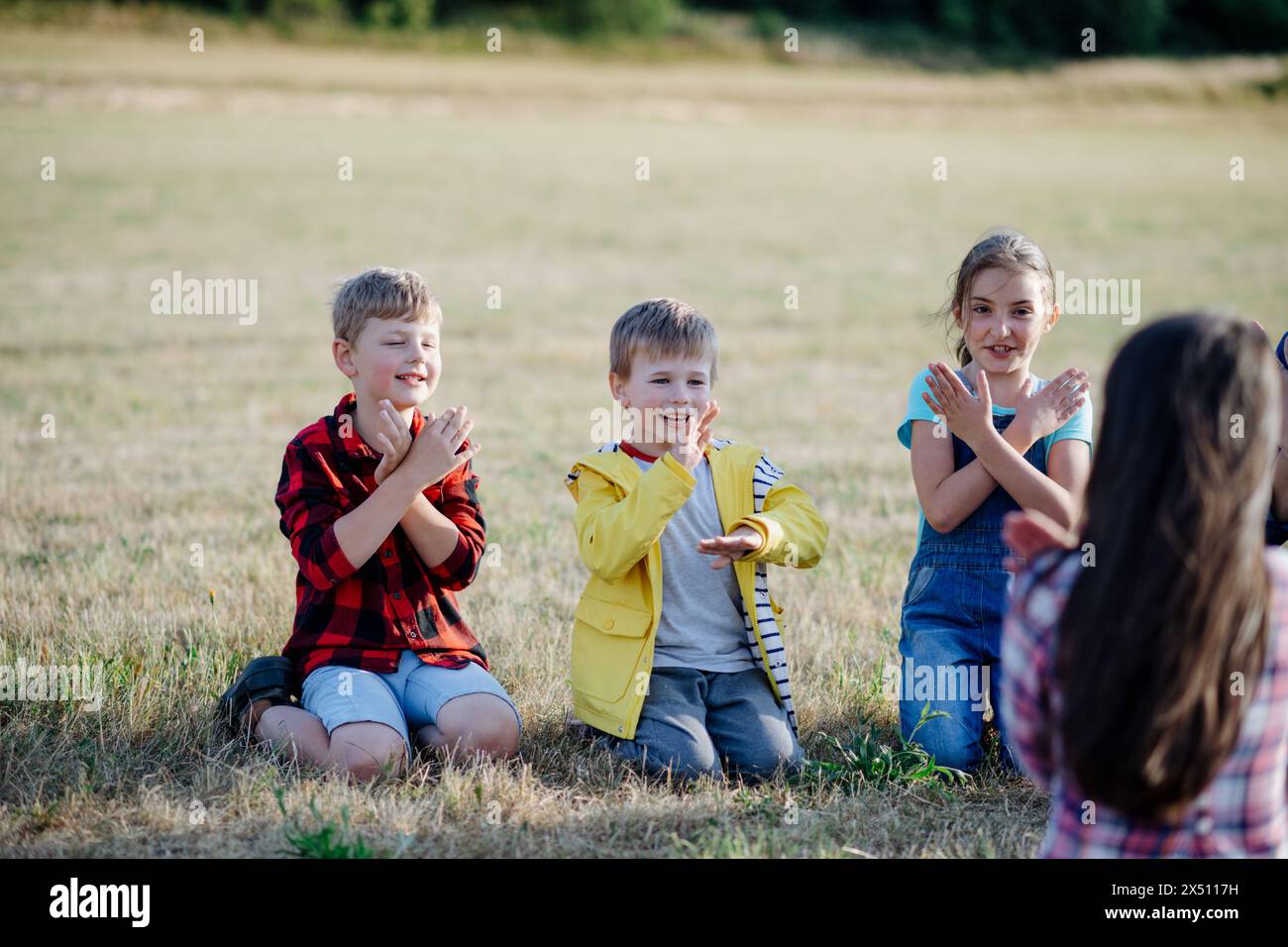 Children sitting on grass on meadow playing clapping game. Dedicated ...