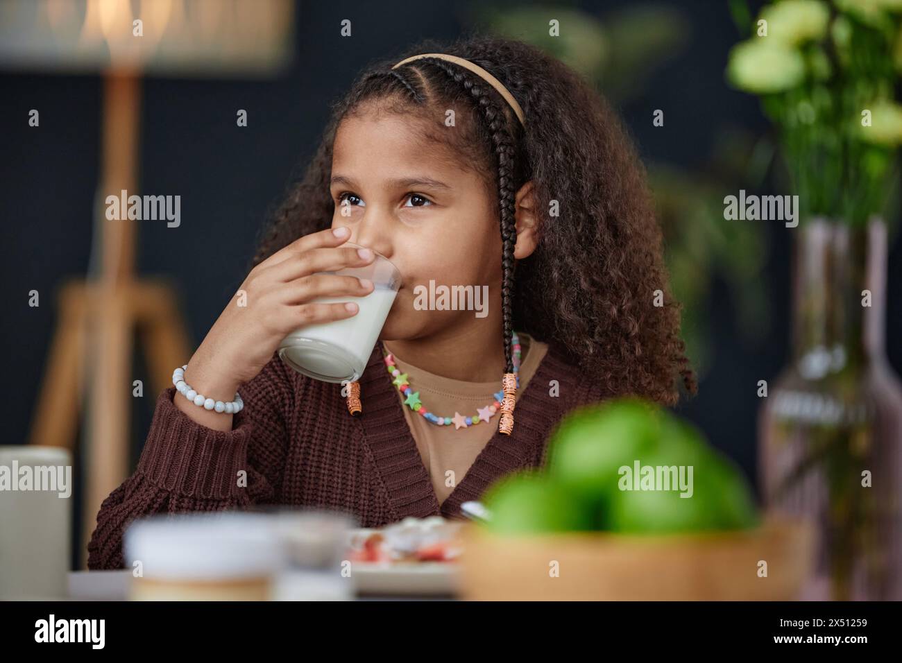 Portrait of teen African American girl drinking milk sitting at dining table during breakfast ...