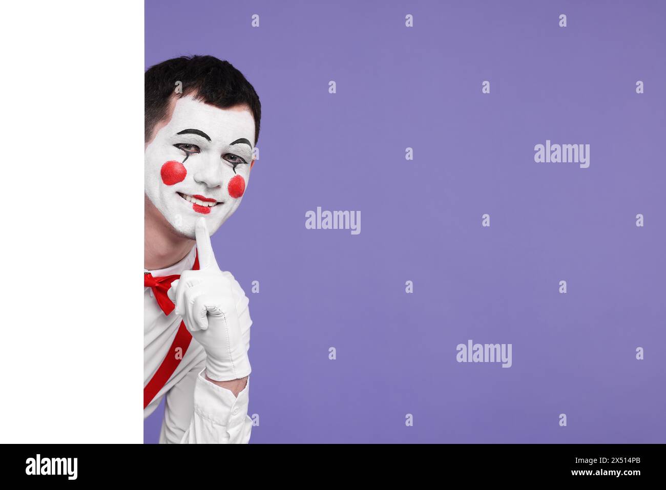 Funny mime artist peeking out of blank poster on purple background ...