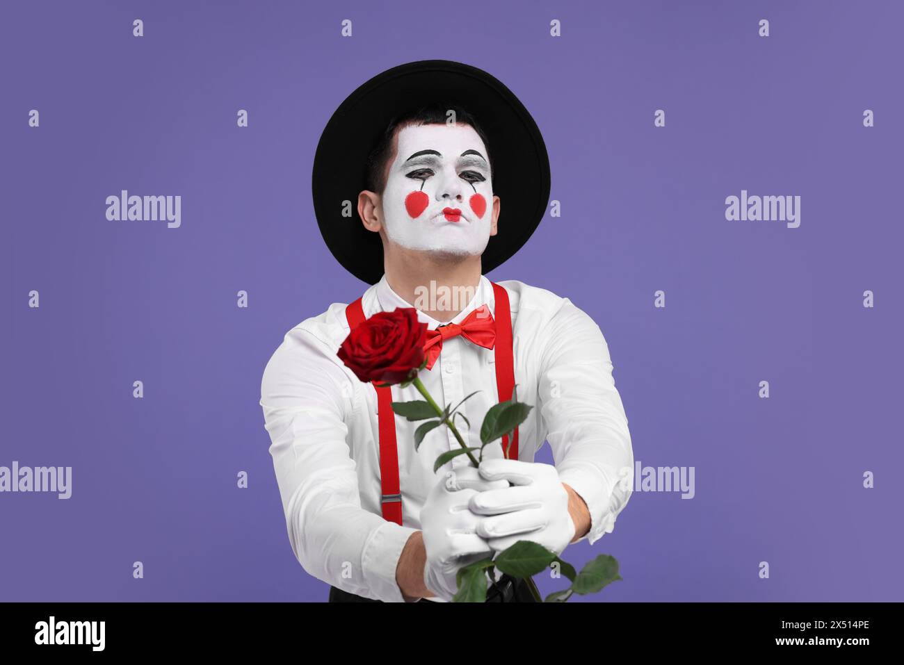 Funny mime artist with red rose on purple background Stock Photo - Alamy