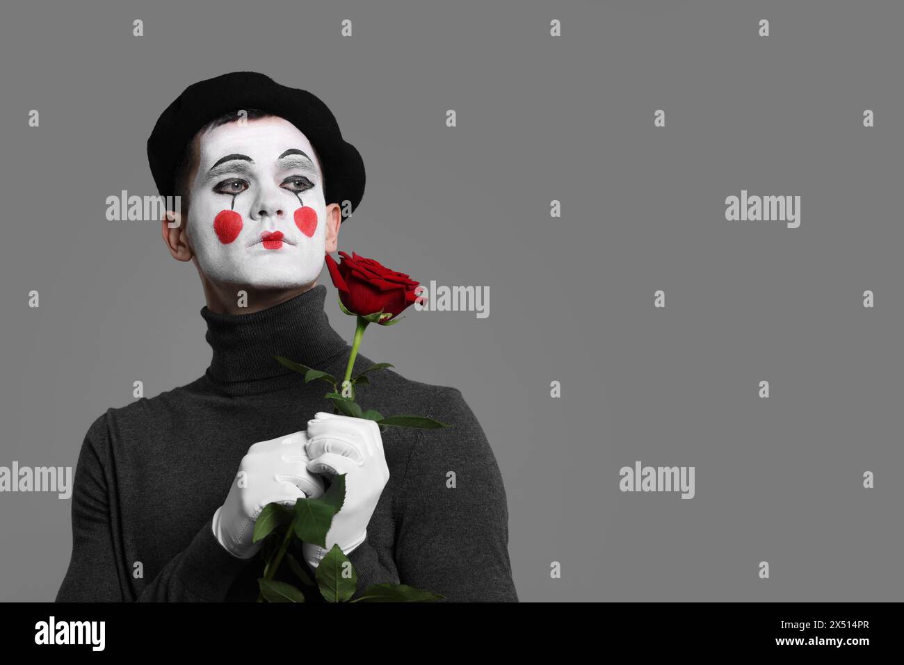 Portrait of mime artist with red rose on grey background. Space for ...