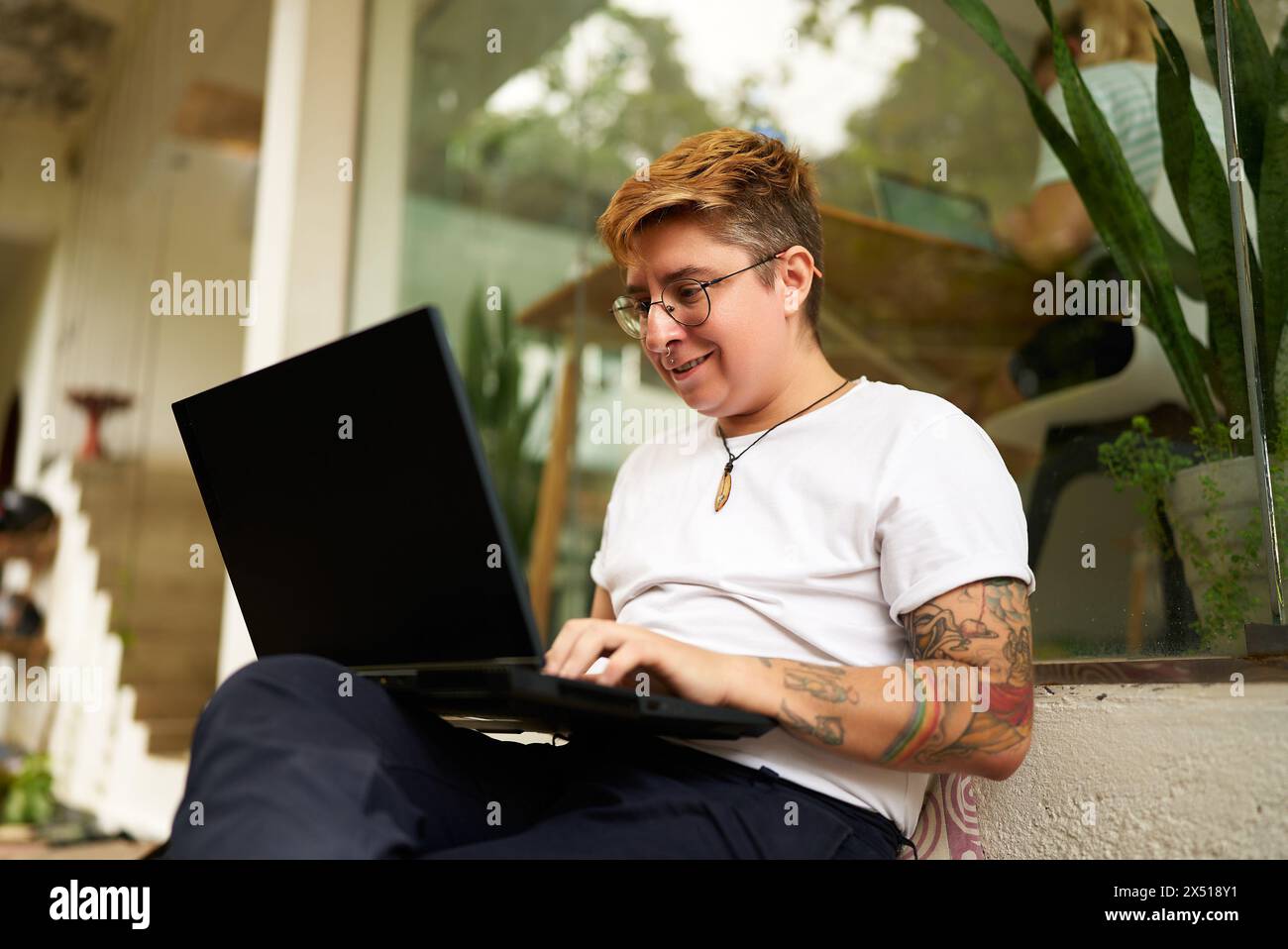 Tattooed Gen Z transgender person works on laptop in cozy office space ...