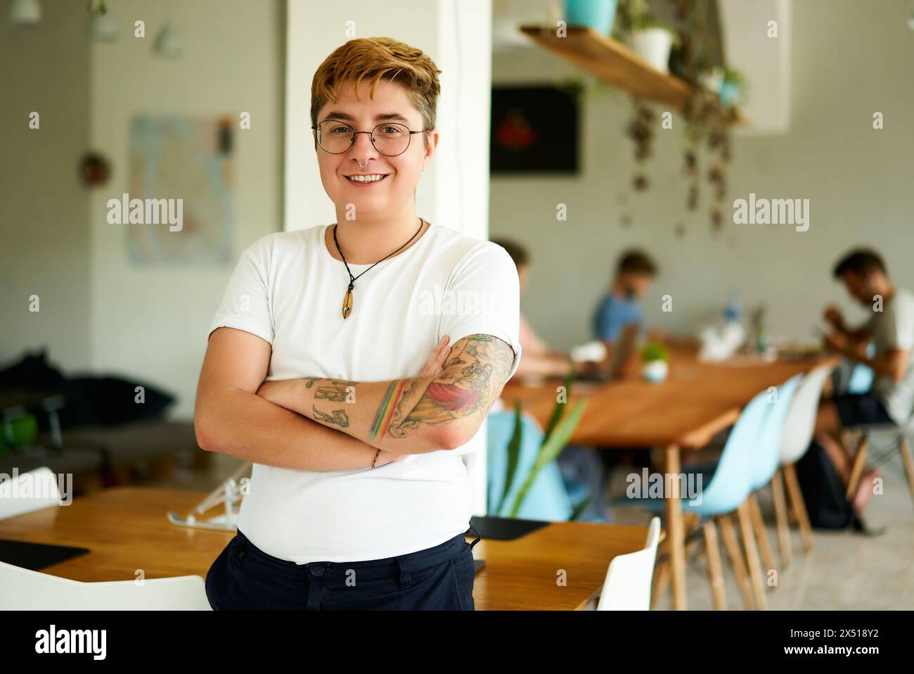 Confident transgender male employee smiling in office space, arms ...