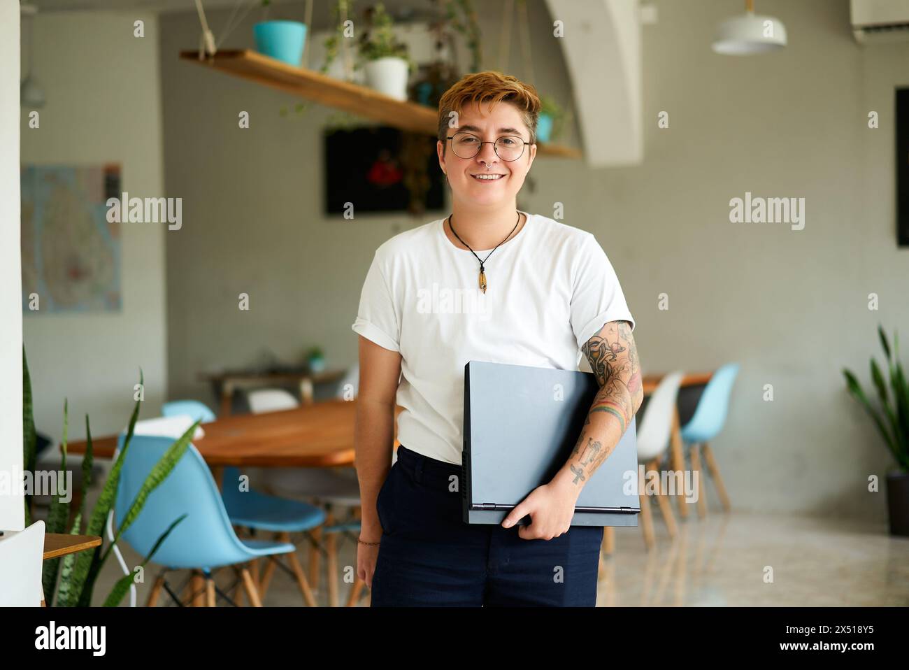 Confident transgender person with tattoos holds laptop, smiles in ...