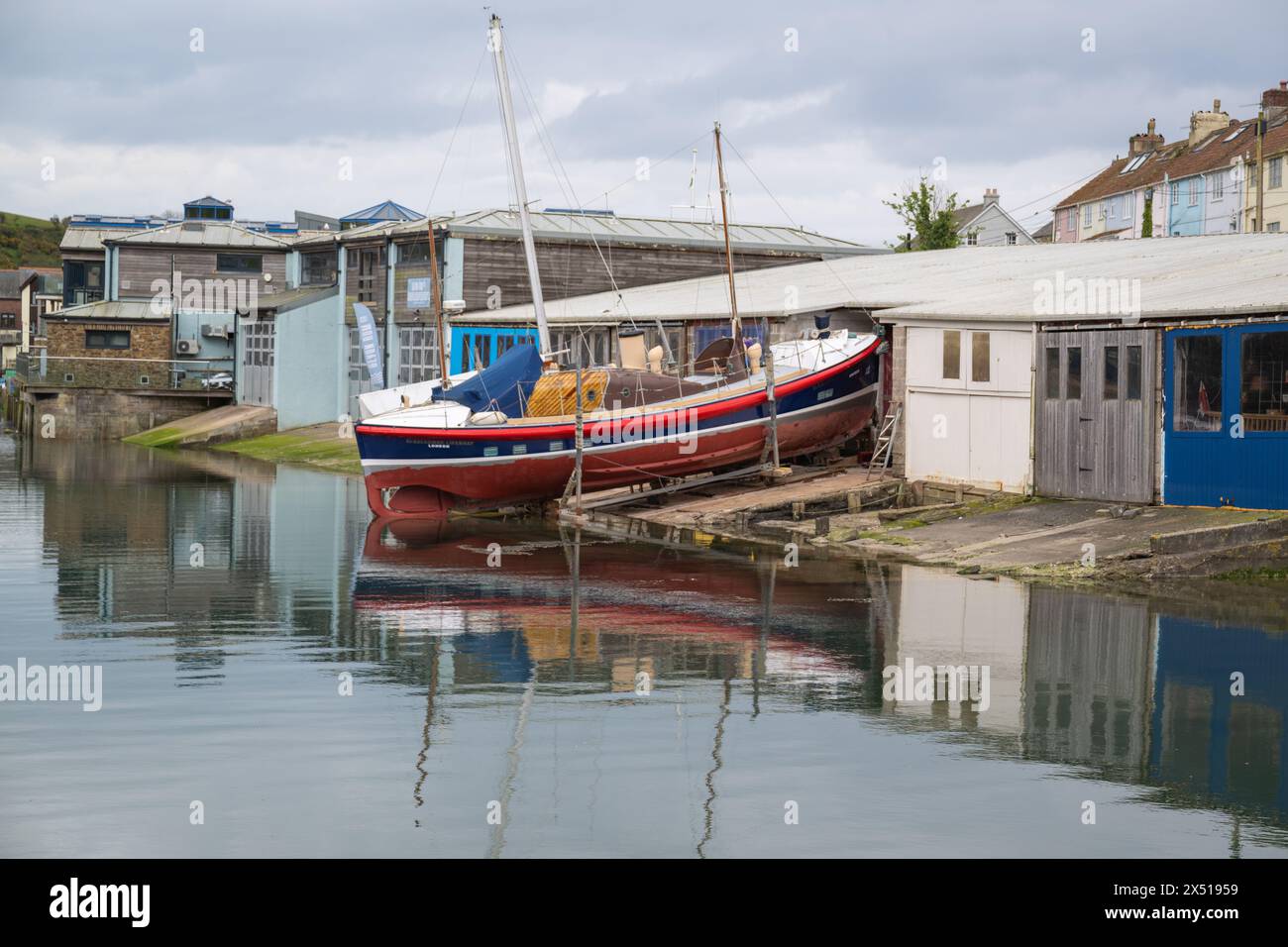 Two masted yacht out of the water on boat ramp next to boat builders ...