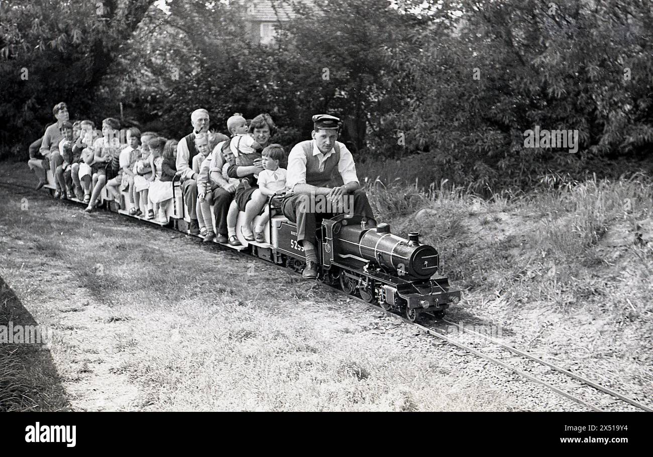 1950s, historical, outside in a park, adults and children having a ride ...