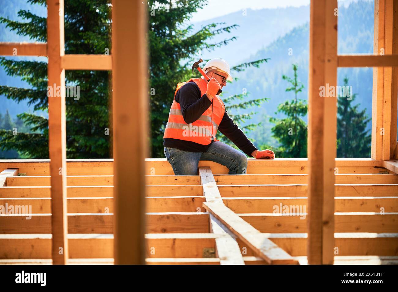 Carpenter constructing two-story wooden frame house near forest. Man ...
