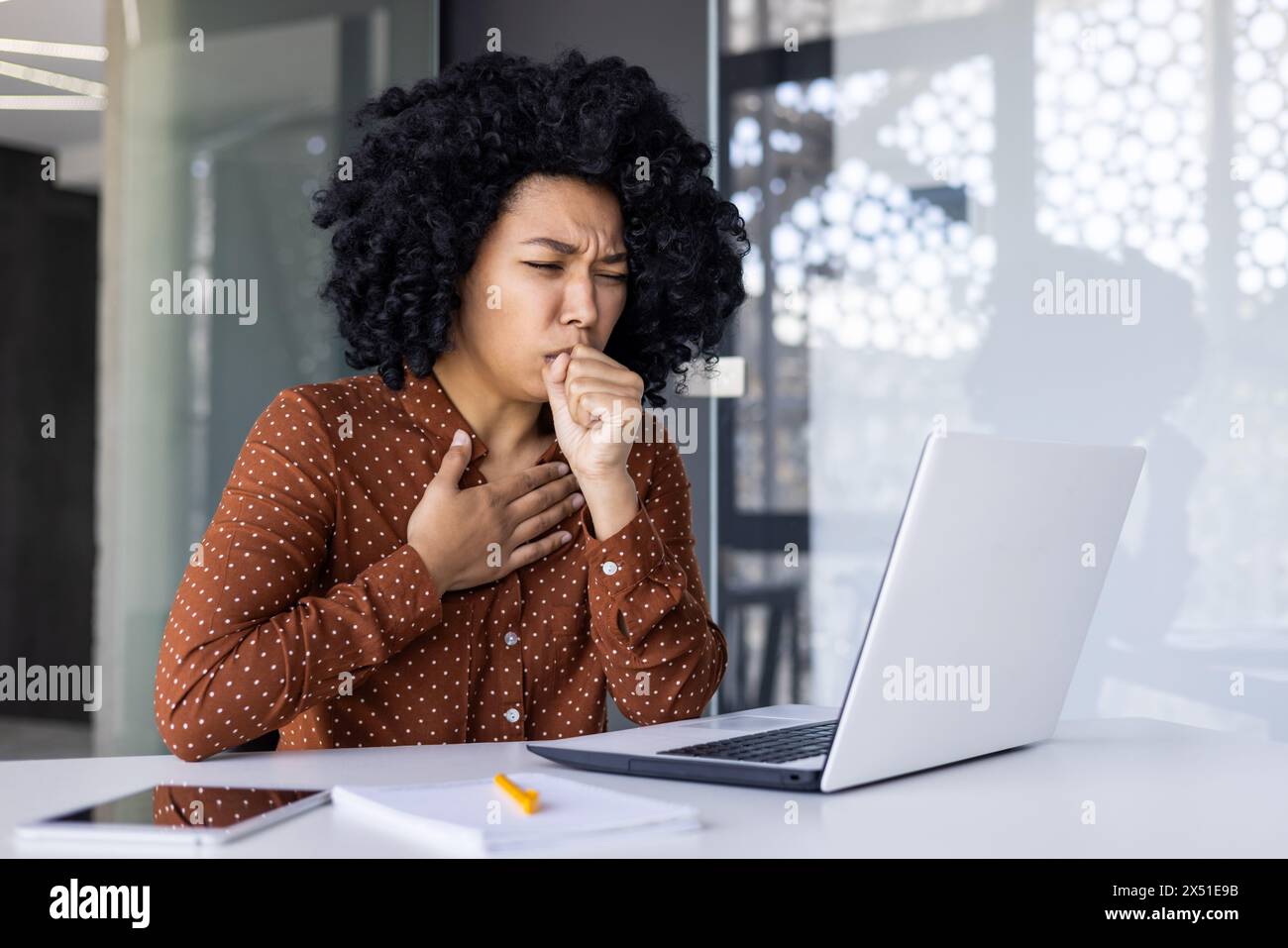 A young African American woman feeling unwell, coughing while working ...