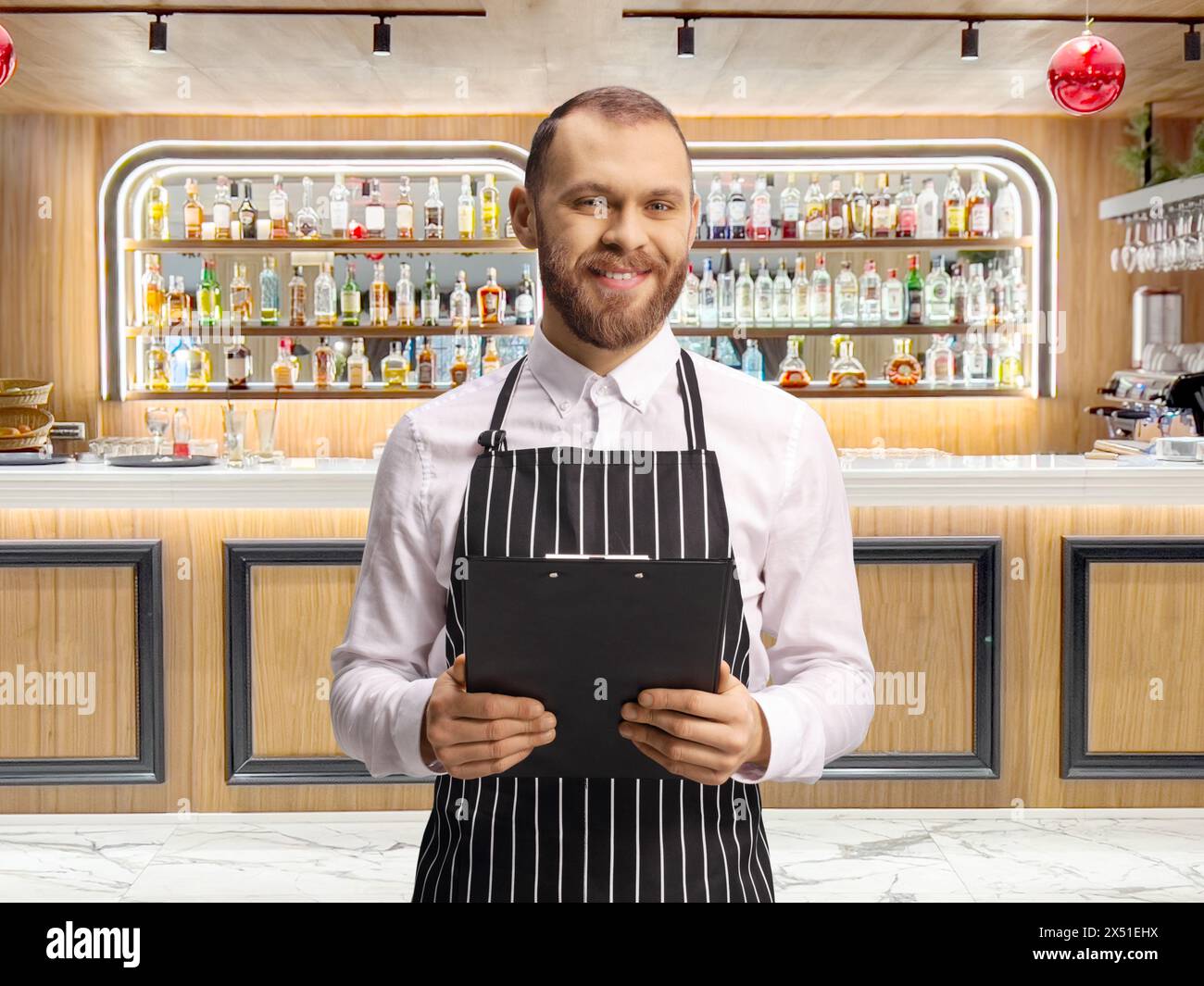 Waiter wearing an apron and holding a menu at a bar Stock Photo - Alamy