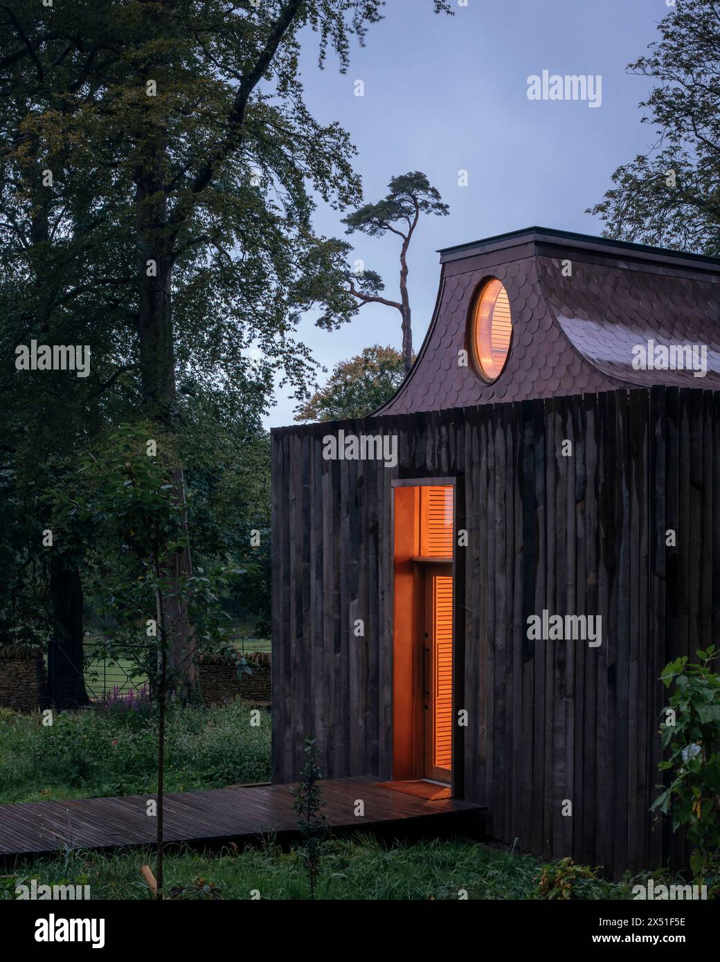 The Apiary pavilion seen at dusk, surrounded by trees. Interior lights ...