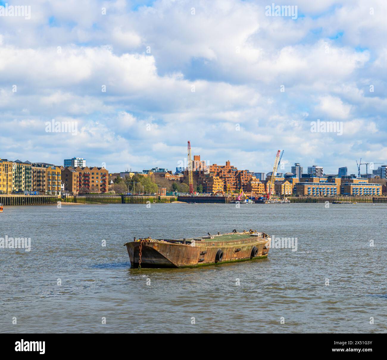 Rusty shipping barge, anchored with a chain and the London Docks seen ...