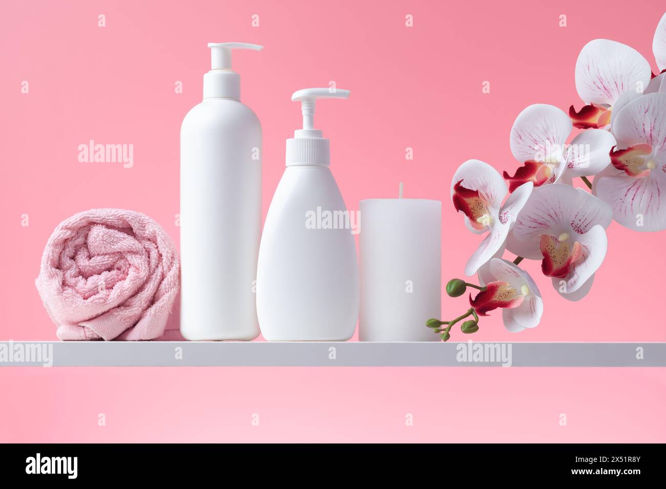 Set of cosmetic bottles, towel, orchid and candle in bathroom. White ...