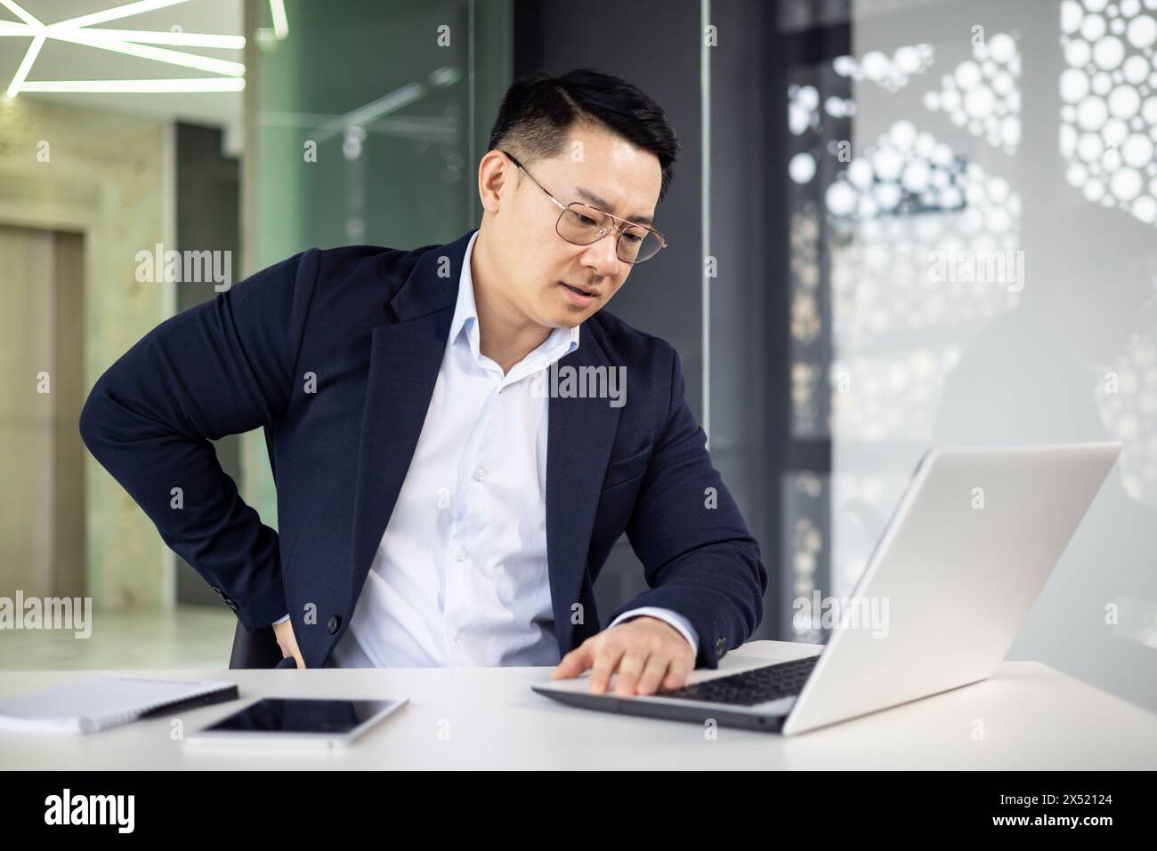Asian businessman in a modern office feeling a sharp pain in his back ...