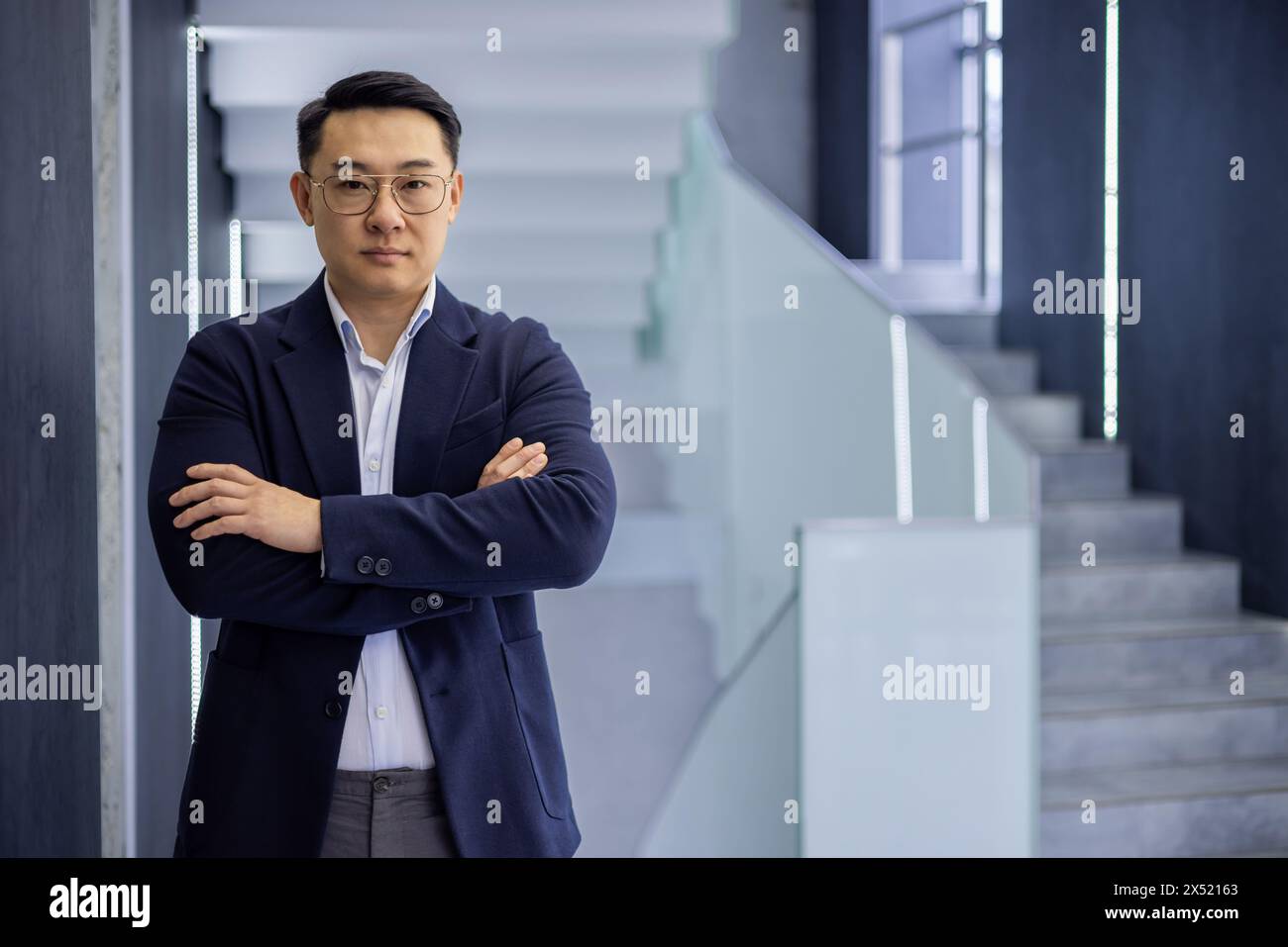 A professional Asian businessman stands confidently with crossed arms ...