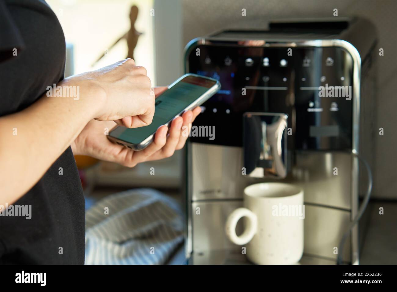 Person uses smartphone app to operate coffee machine. Woman preparing ...