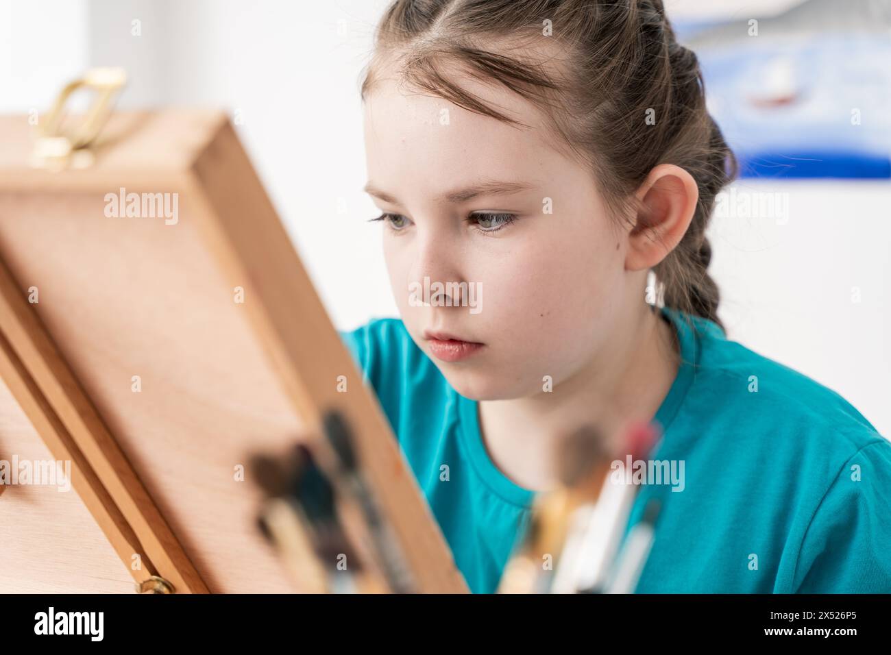 Little girl of pre-adolescence drawing on easel. Beautiful little girl ...
