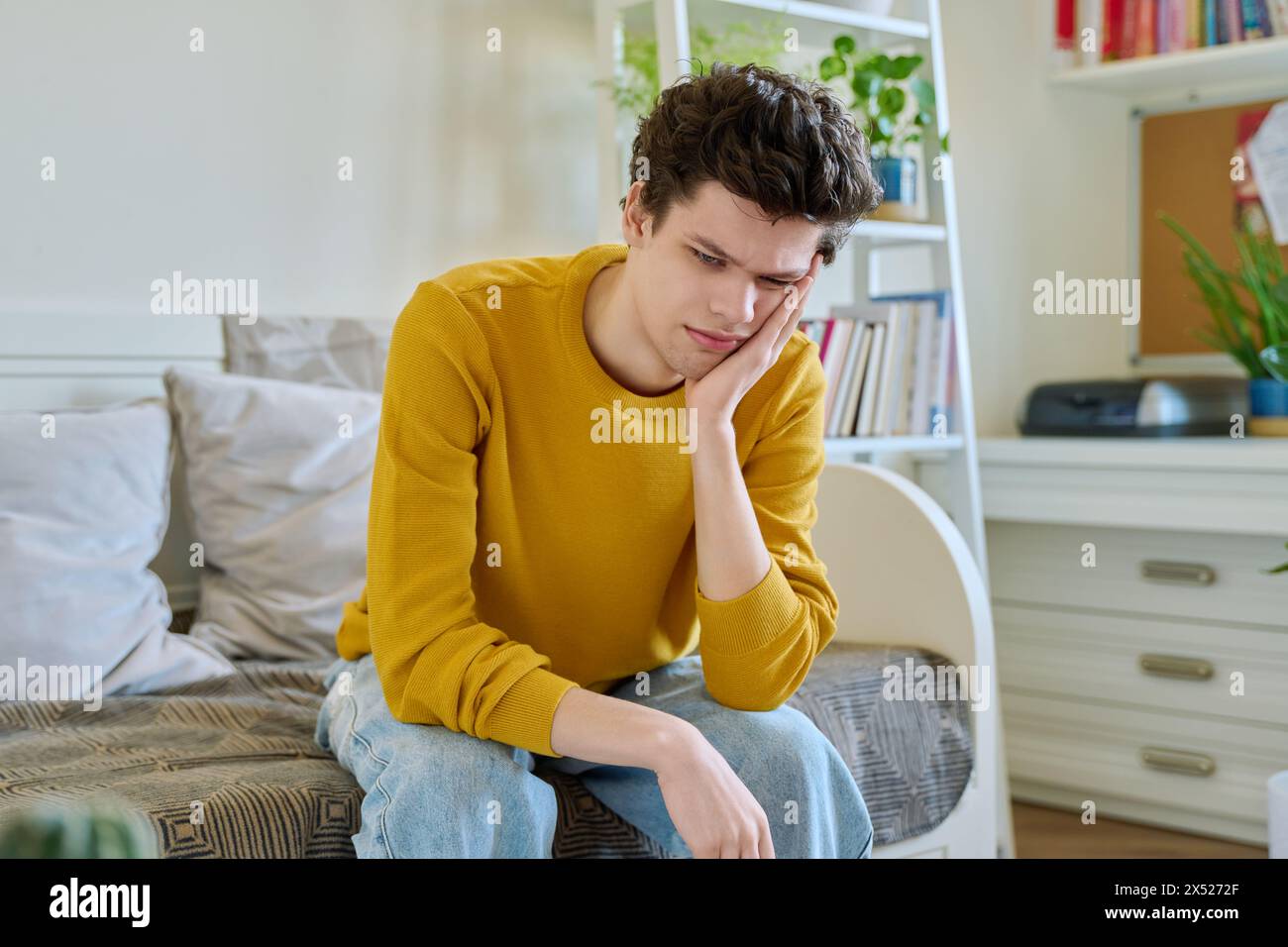Sad upset young man sitting on couch at home, touching his head with ...