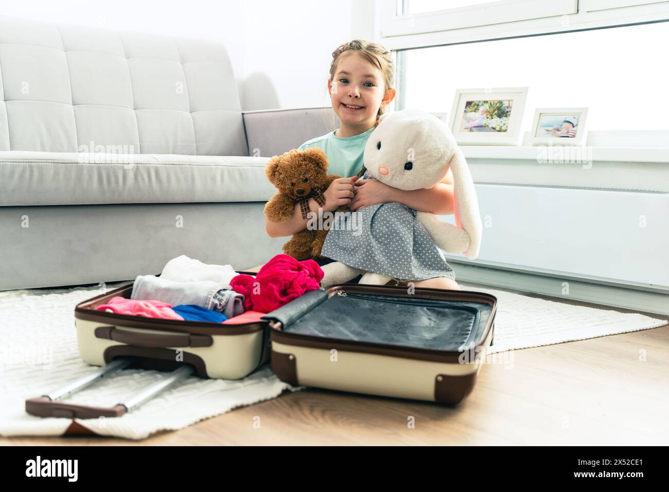 Happy little girl packing suitcase for travel while sitting at home ...