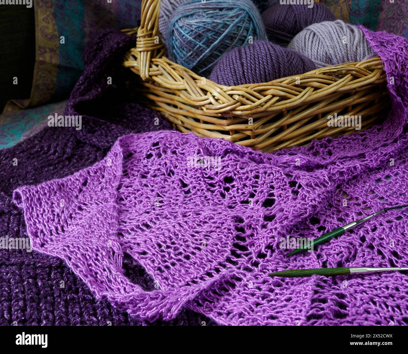 Purple knitted shawl with basket of yarn in background Stock Photo - Alamy
