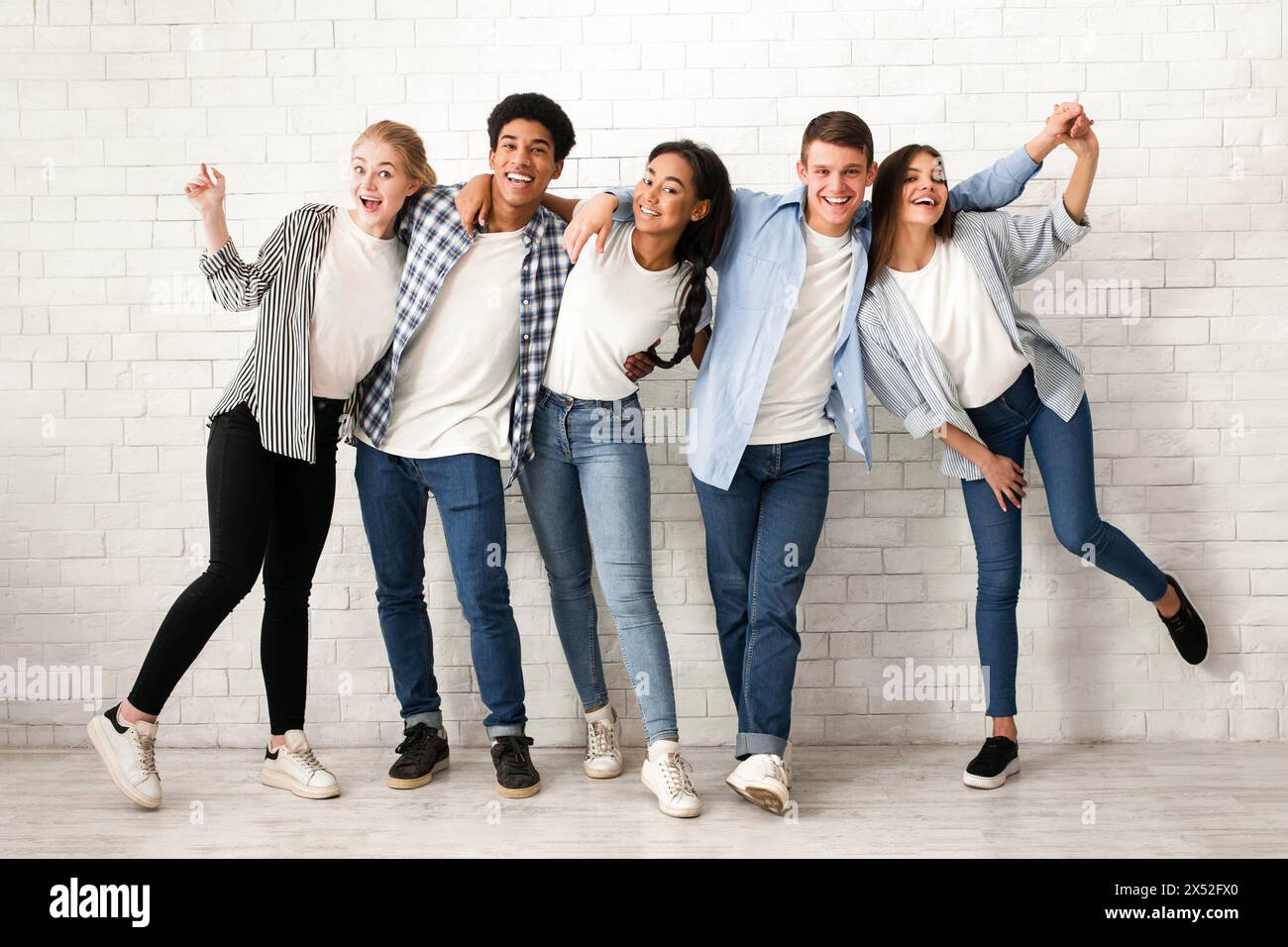 Friends Posing Happily Together Against White Brick Wall During ...