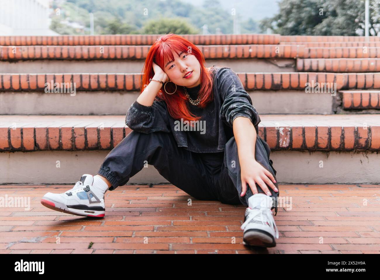 Relaxed Korean woman with red hair resting on city steps, hand on head ...