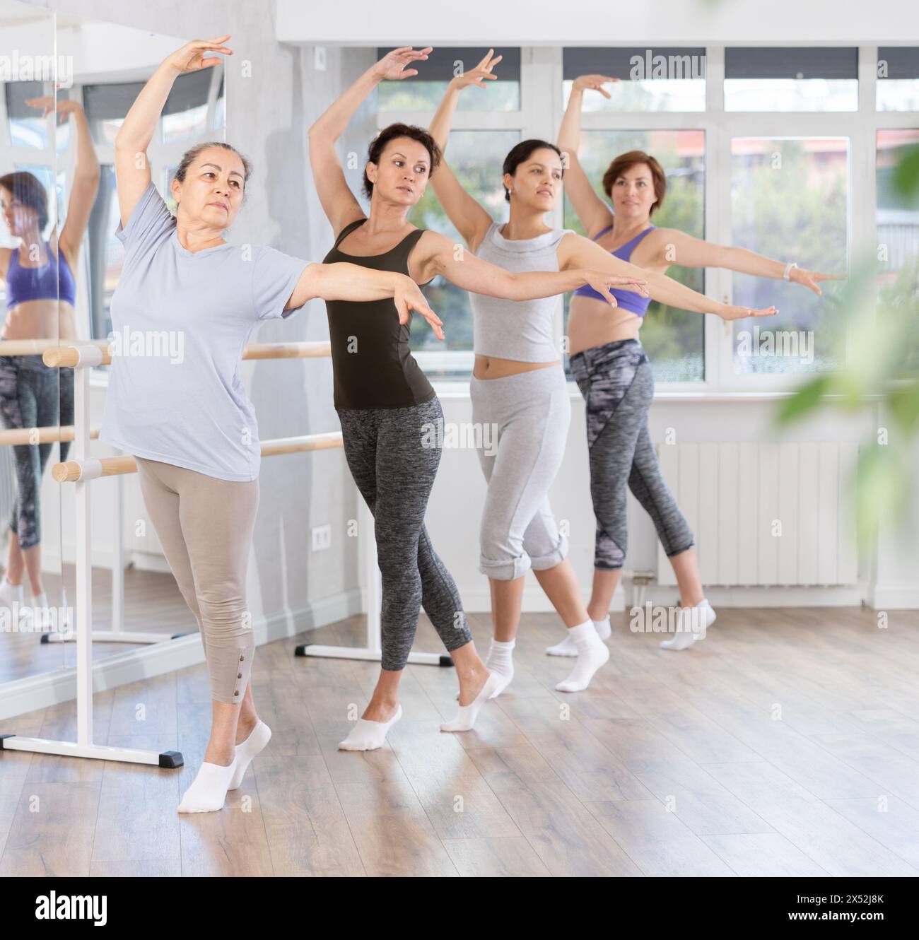 Female ballet dancers doing various ballet movements at ballet barre in ...