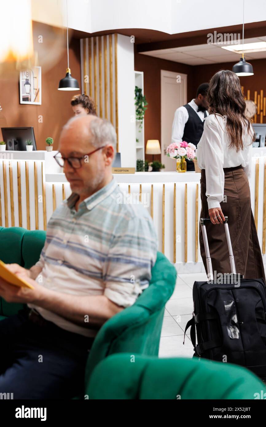 Caucasian elderly lady with luggage enters contemporary hotel lobby and ...