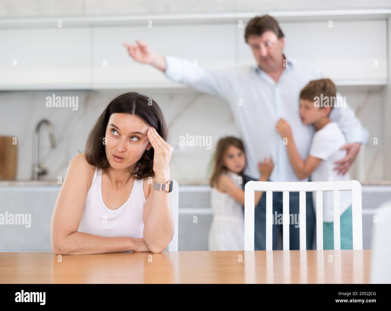 Sad mom is sitting near table in kitchen and listens to abuse of angry ...