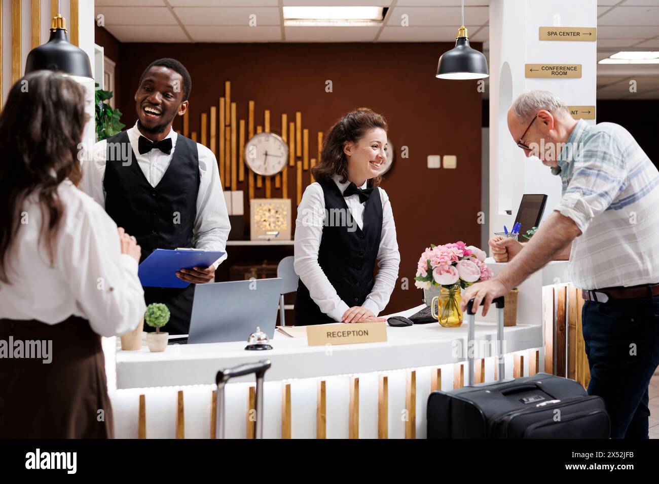 Retired senior couple arrive at hotel, assisted by smiling multiethnic ...