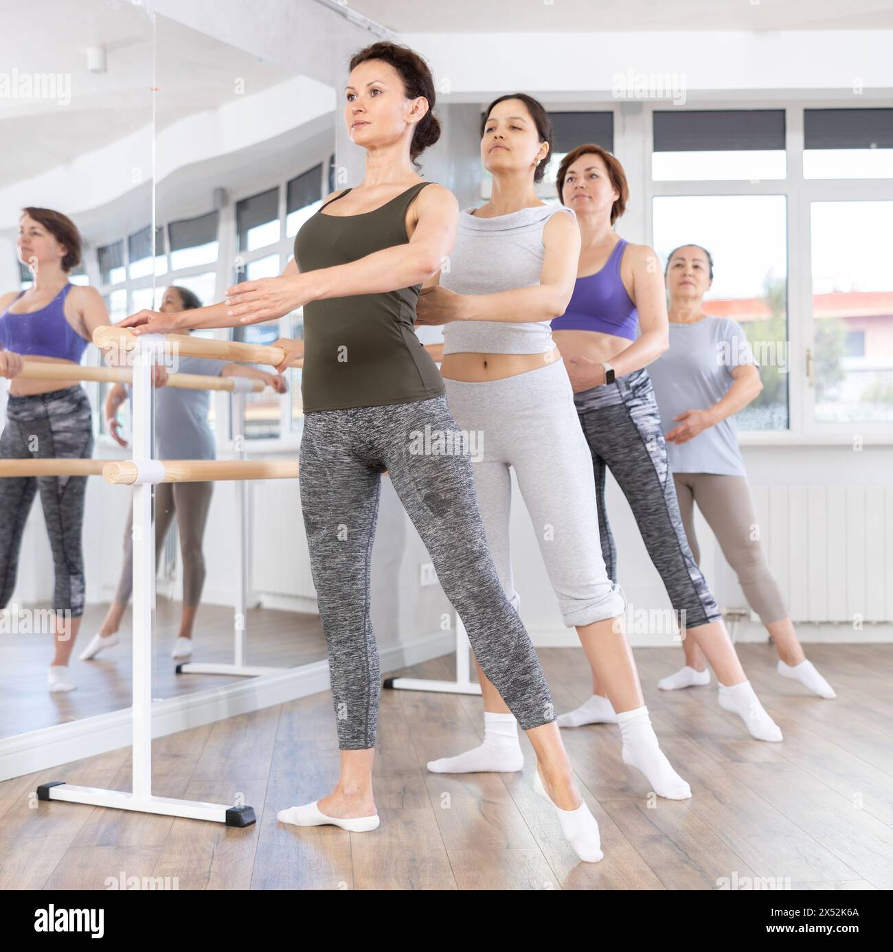 Woman performing battement tendu at ballet barre at beginners group ...