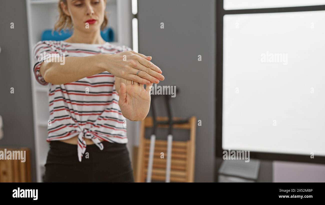Young woman stretching wrist in clinic rehab room, conveying health ...