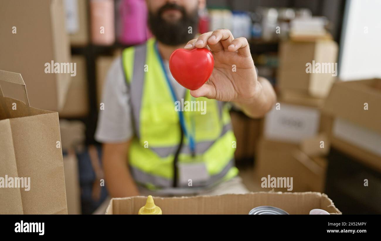Hispanic man in warehouse holds red heart, conveying care and charity ...