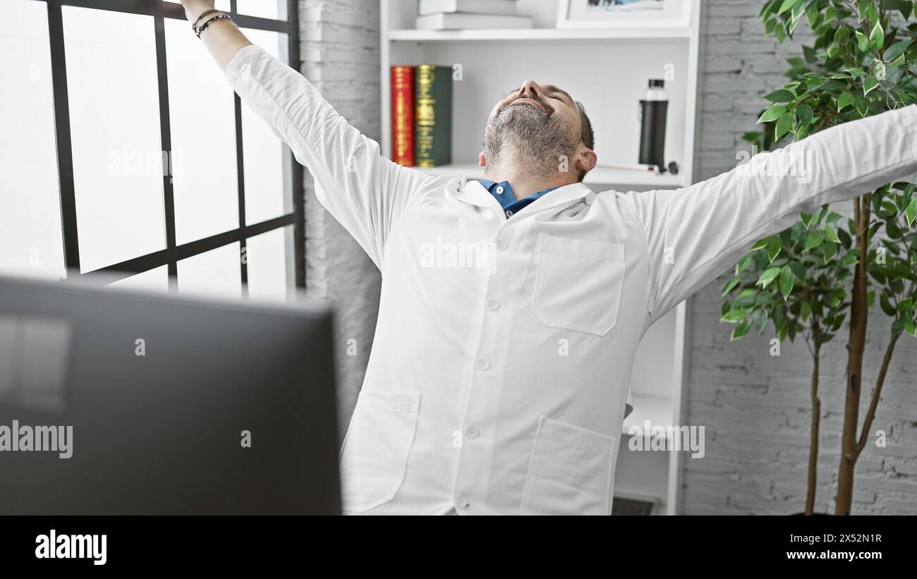 Hispanic mature man in white lab coat stretching indoors, depicts a ...