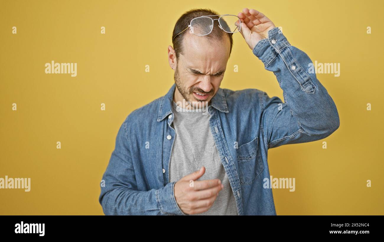 Hispanic bald man with beard in denim shirt holding glasses against a ...
