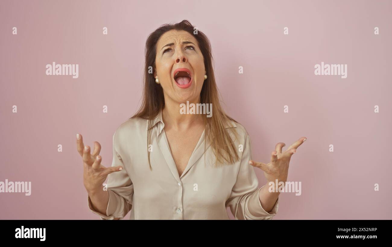 A frustrated young woman gestures despair against a plain pink ...