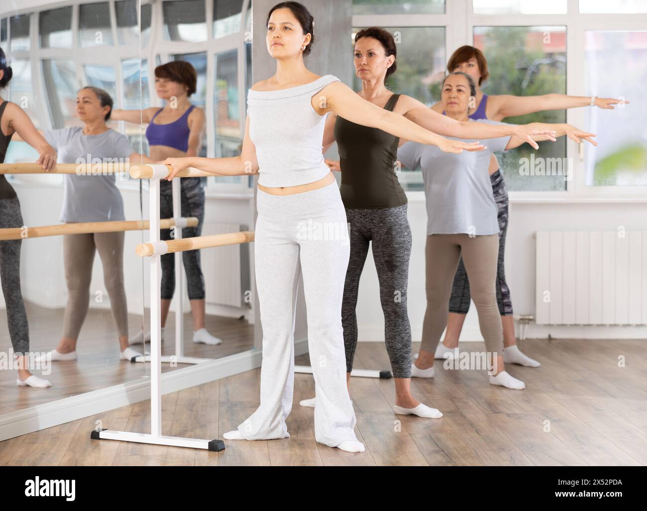 Women of different ages exercise near the ballet barre at group ...