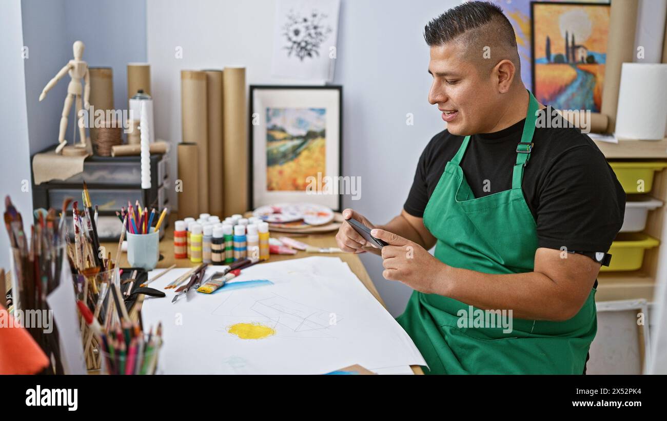 Young, confident latin artist guy making smartphone photos of his art ...
