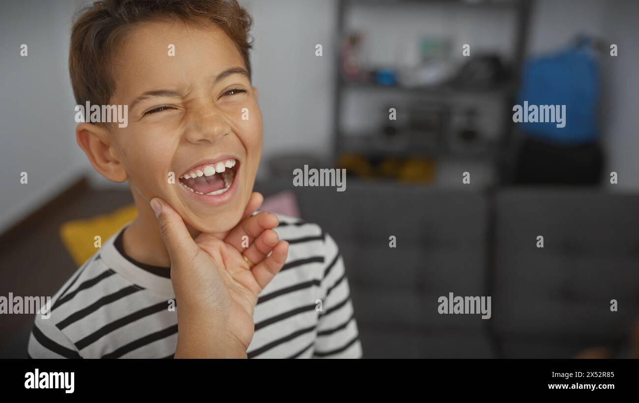 Laughing boy with hand on cheek, striped shirt, in a modern home ...