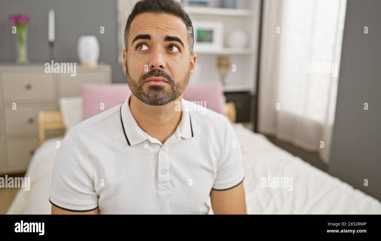 Pensive hispanic man with beard in a modern bedroom interior ...