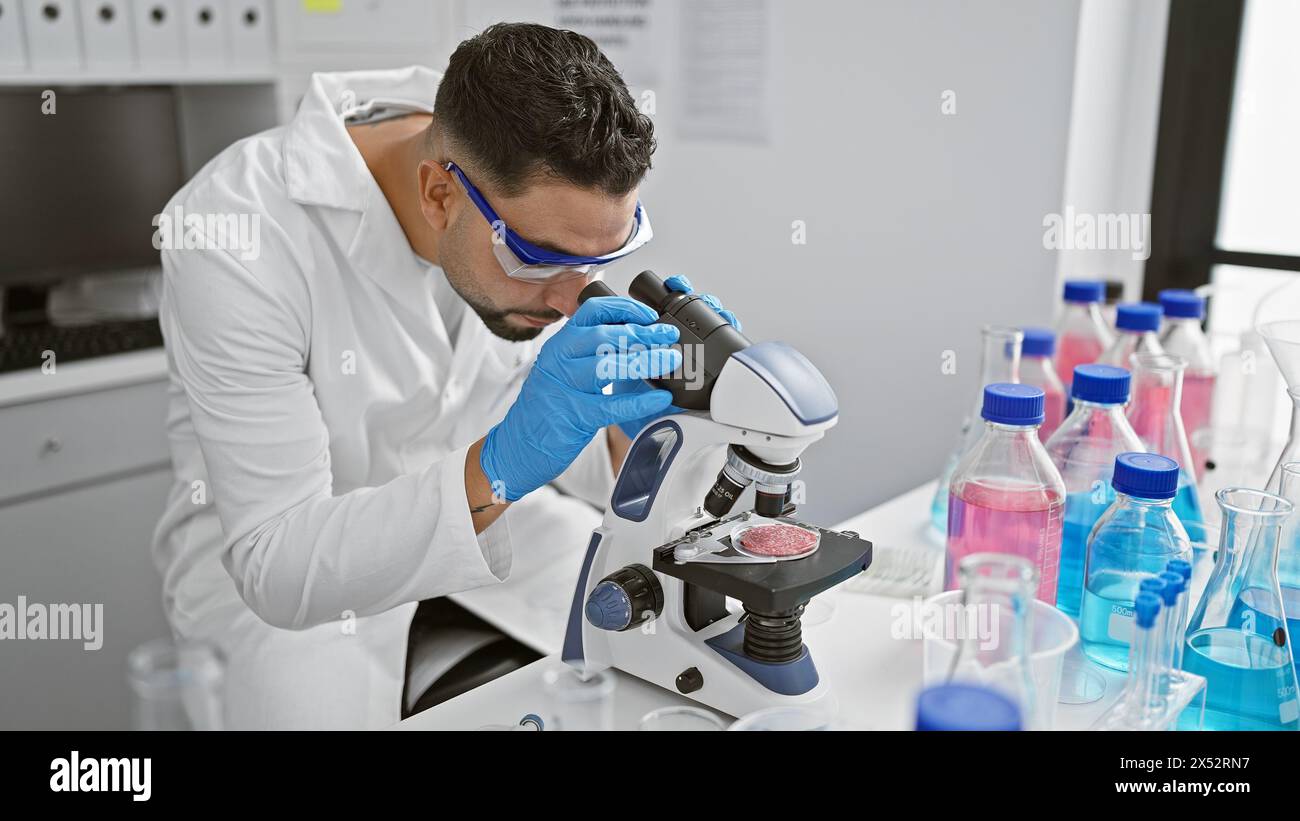 A young man examines a specimen under a microscope in a laboratory ...