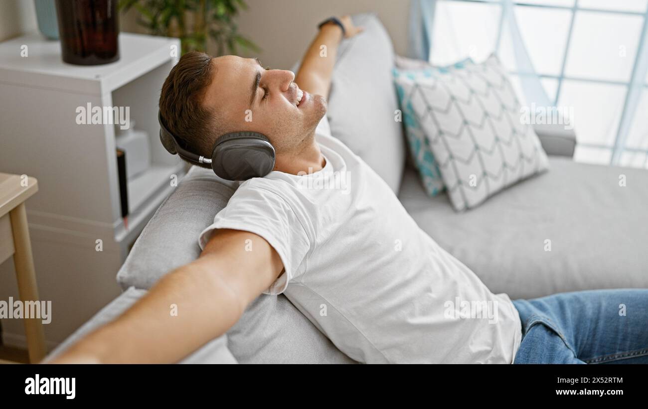A relaxed young man wearing headphones reclining on a sofa with a ...
