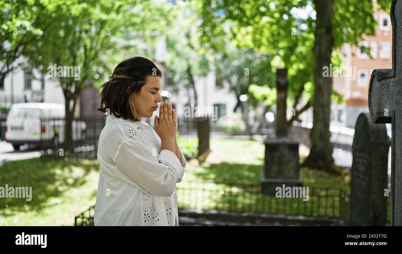 Beautiful young hispanic woman praying and mourning by tombstone at ...