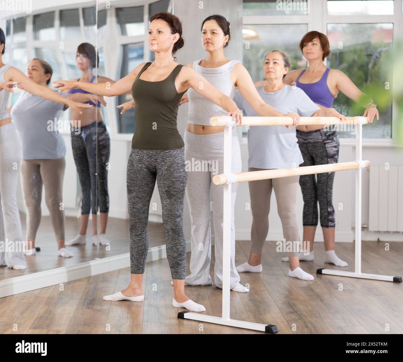 Women of different ages exercise near the ballet barre at group ...
