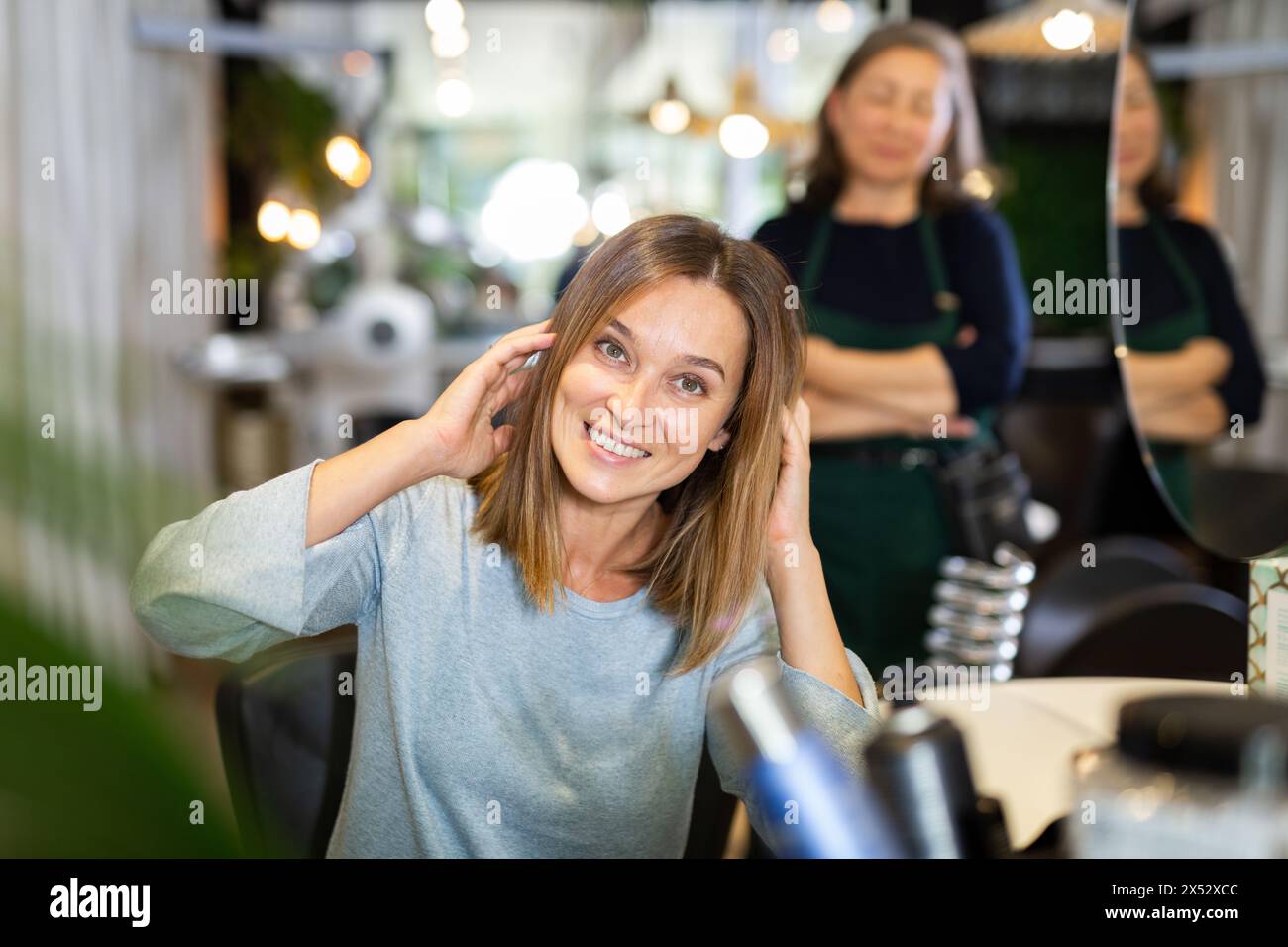 Delighted female client sitting in hairdressing chair after haircut ...