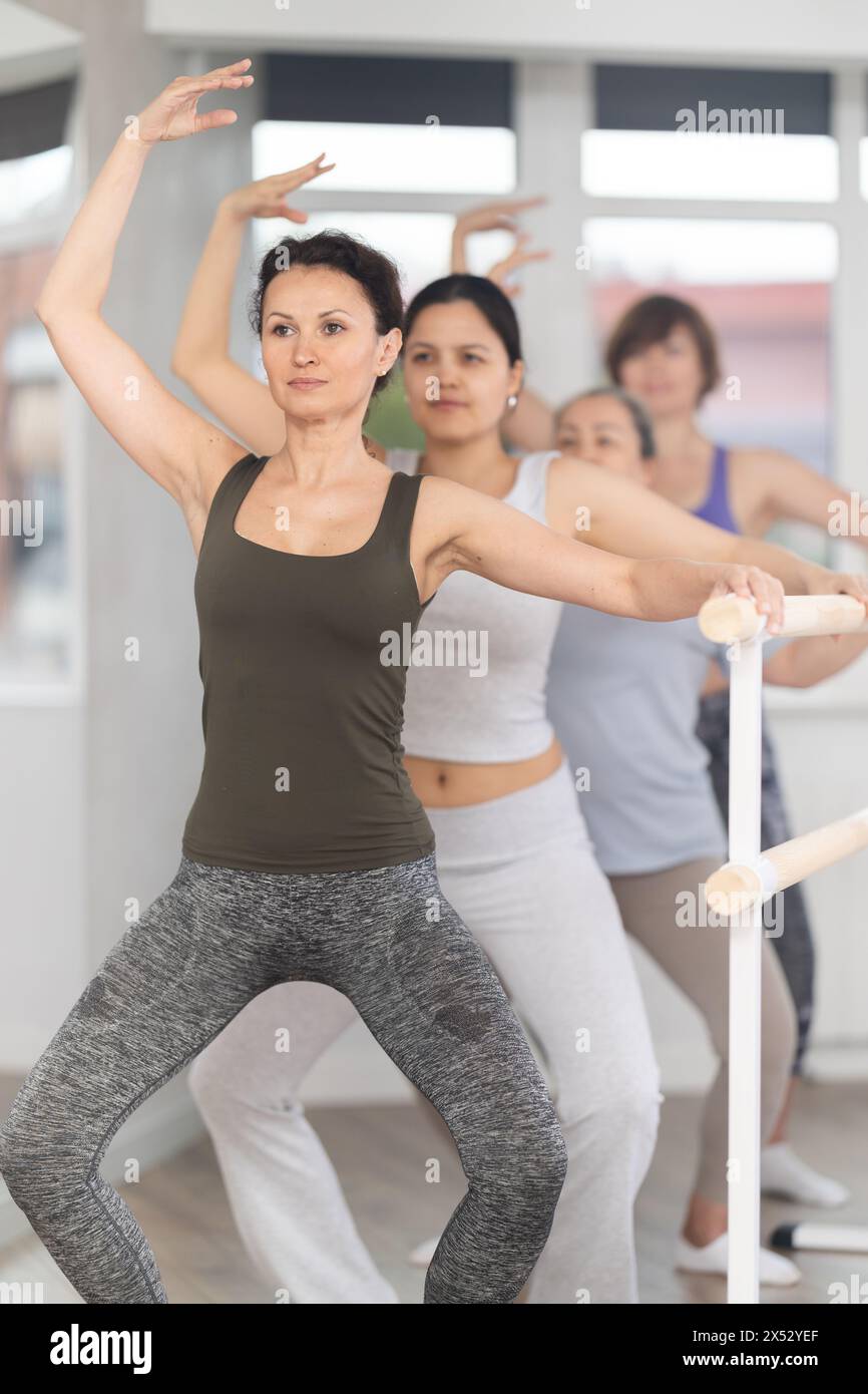 Woman performing demi plie in group barre session in fitness studio ...