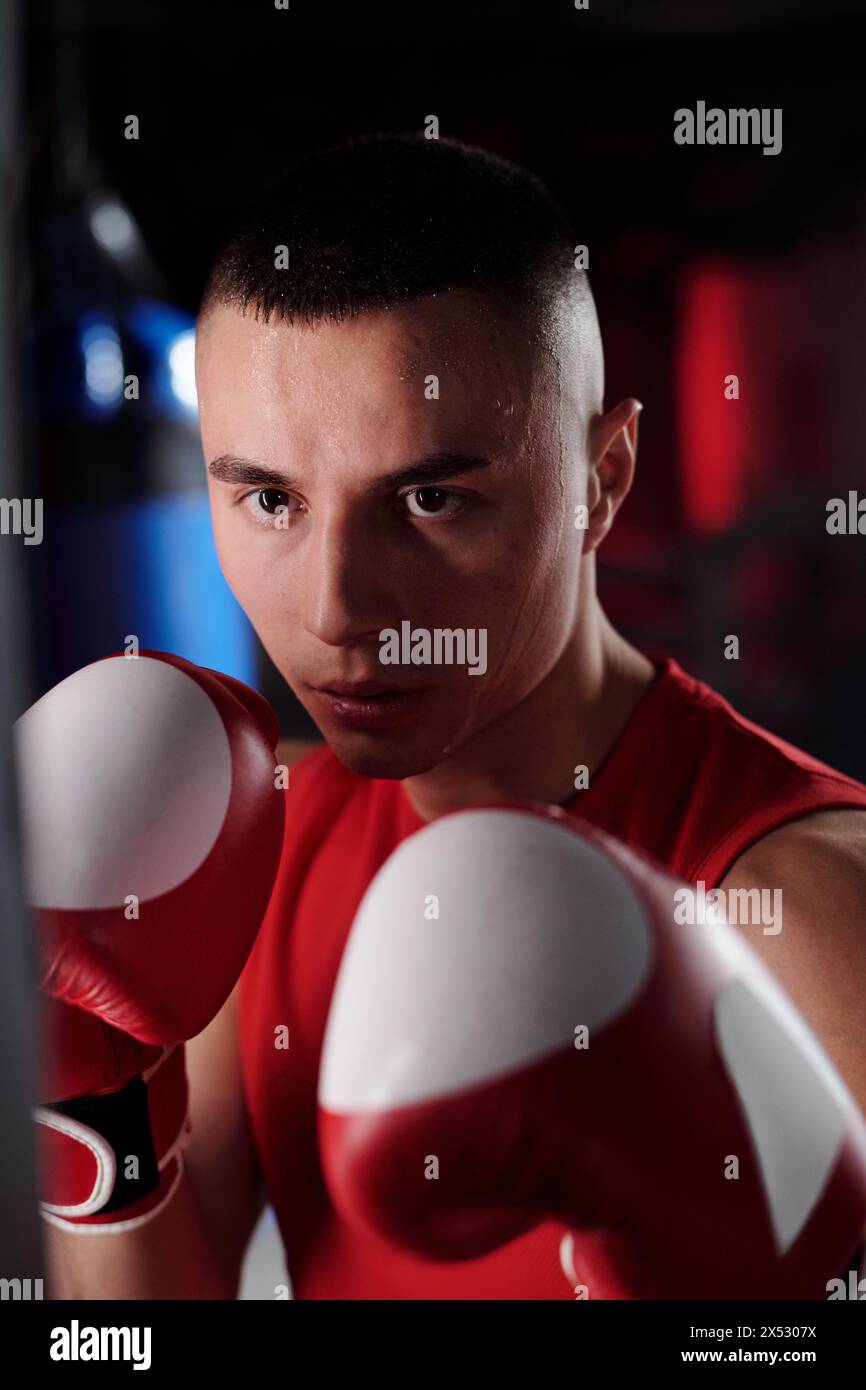 Young professional boxer in red vest standing in front of punching bag ...